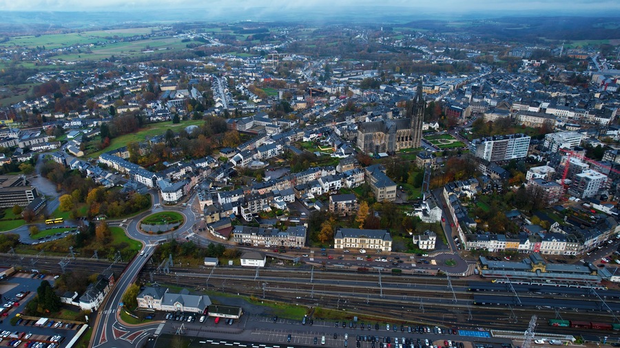 Vista aérea de uma cidade com uma catedral imponente, estação ferroviária e áreas residenciais densas.