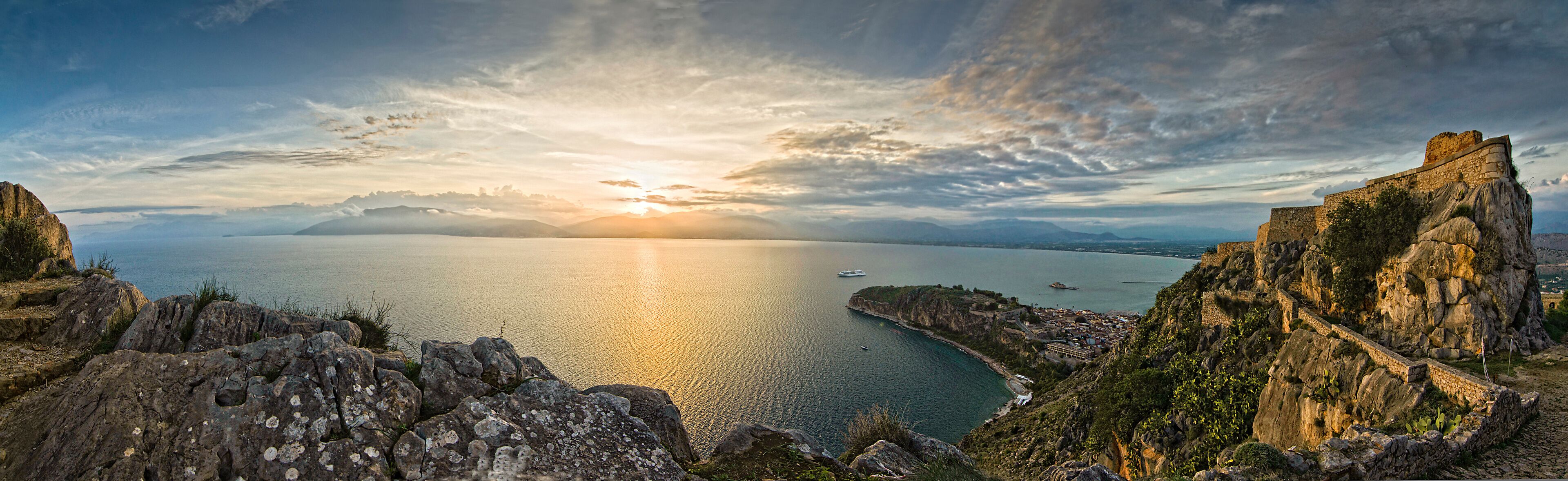 Paisagem costeira com falésias rochosas, mar calmo e pôr do sol.