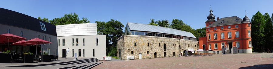 Um museu com guarda-sóis vermelhos, um edifício moderno, uma estrutura de pedra e um edifício histórico vermelho com uma torre.