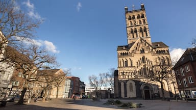 Igreja histórica com uma torre alta, rodeada por edifícios urbanos e árvores sem folhas.