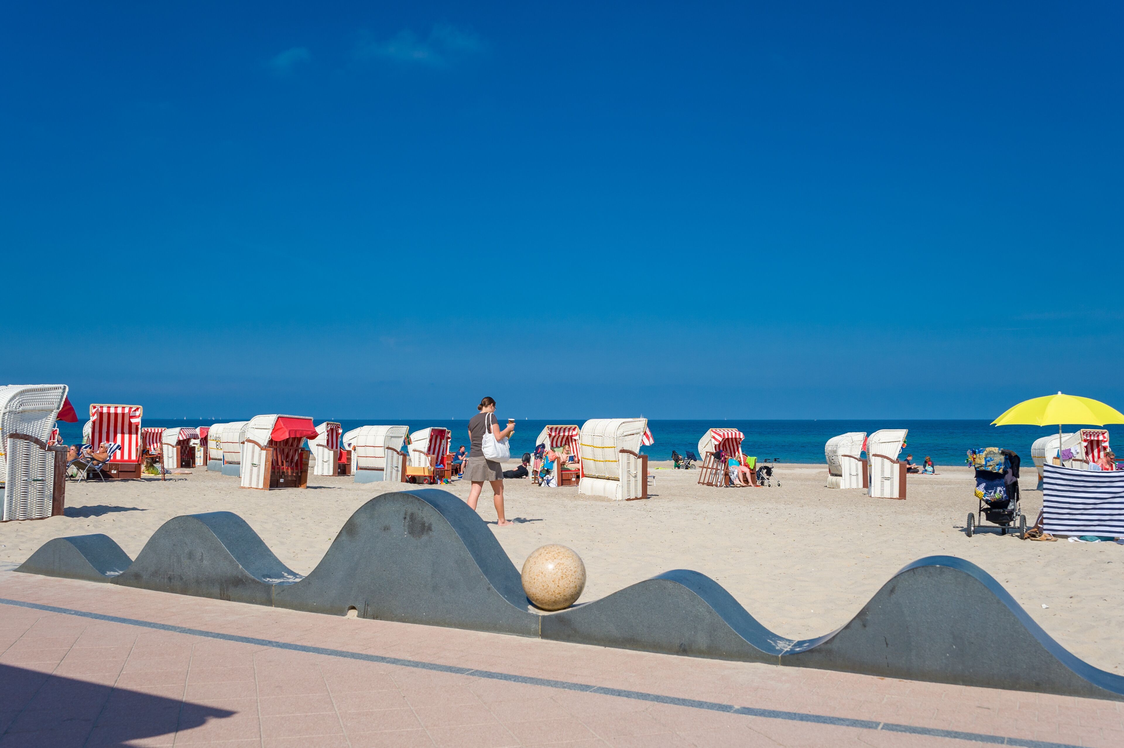 Uma praia com cadeiras de praia, guarda-sóis e um céu azul límpido.