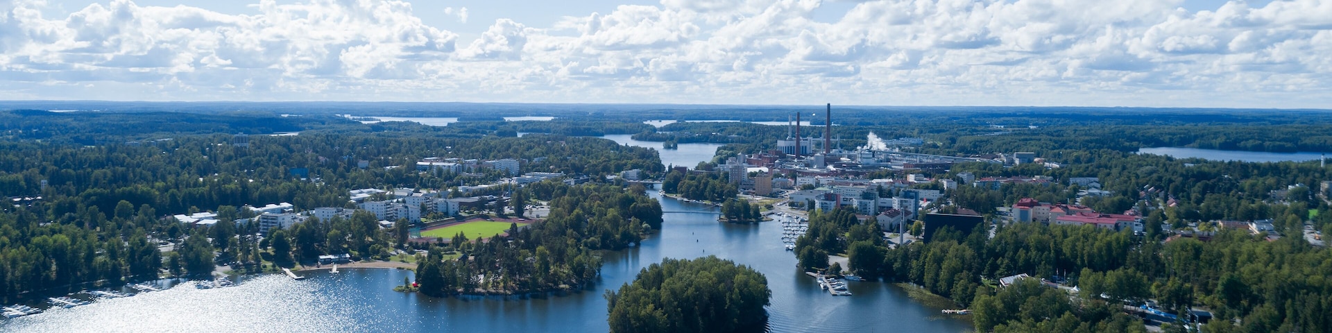 Um lago rodeado por floresta e áreas urbanas, com edifícios e uma chaminé alta.