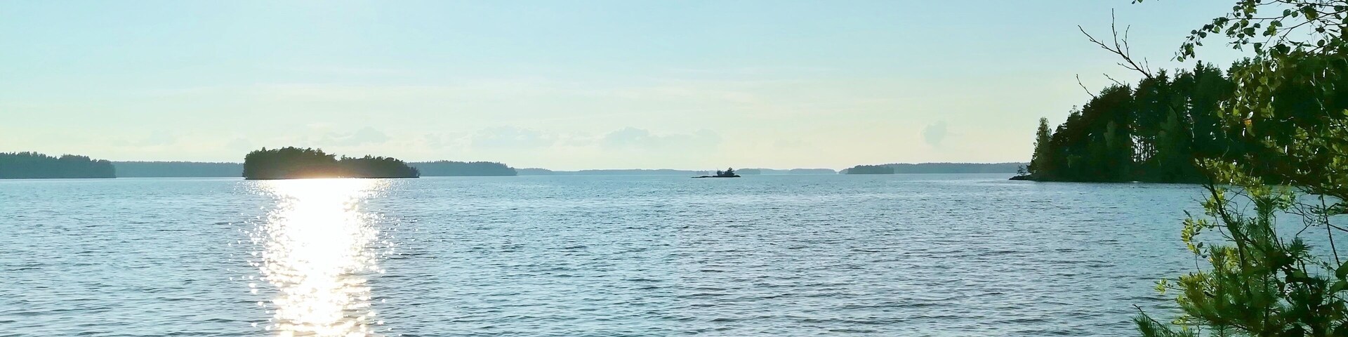 Um lago tranquilo com uma pequena ilha ao longe, rodeado por árvores.