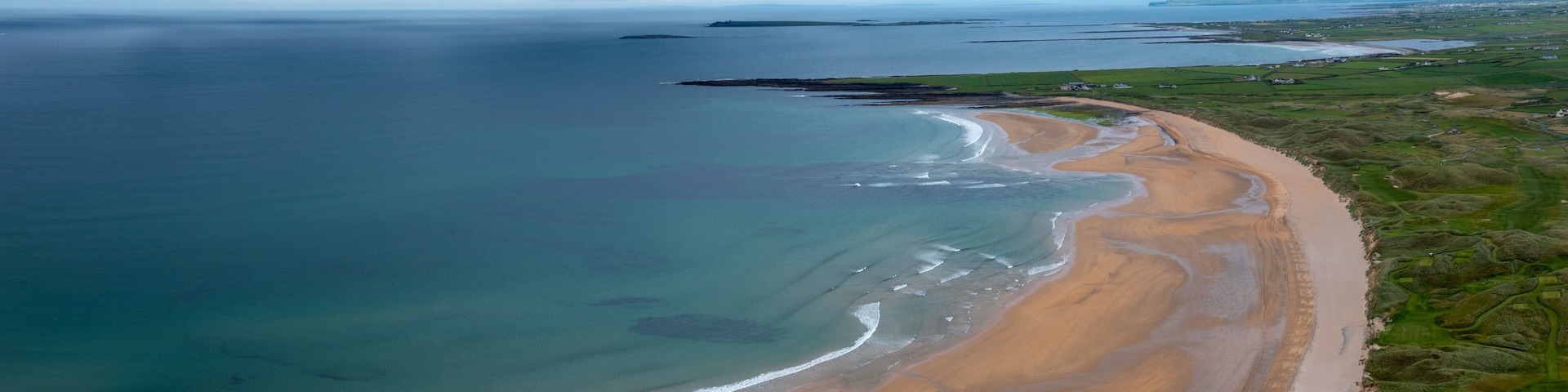 Paisagem costeira com uma praia de areia, mar calmo e céu nublado.