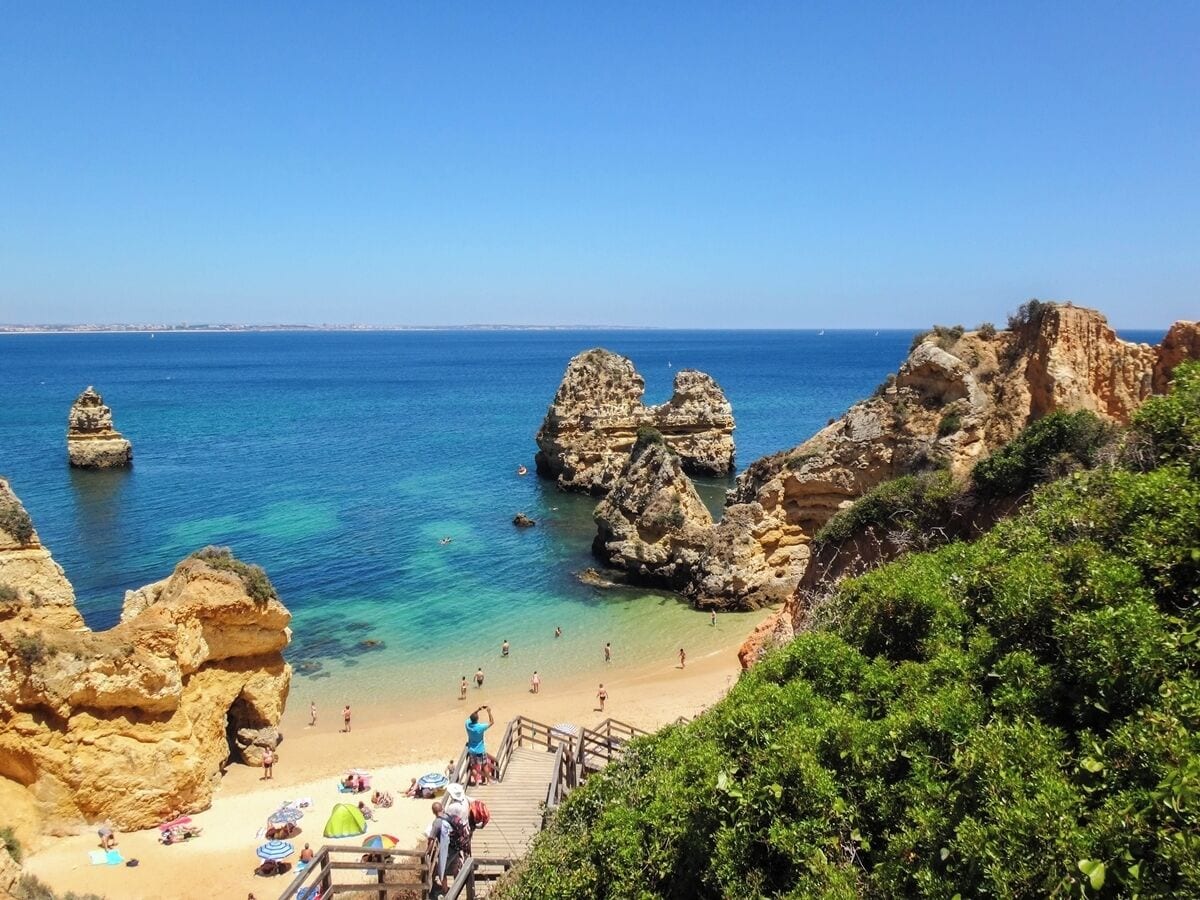 Uma praia costeira com formações rochosas e água azul cristalina.