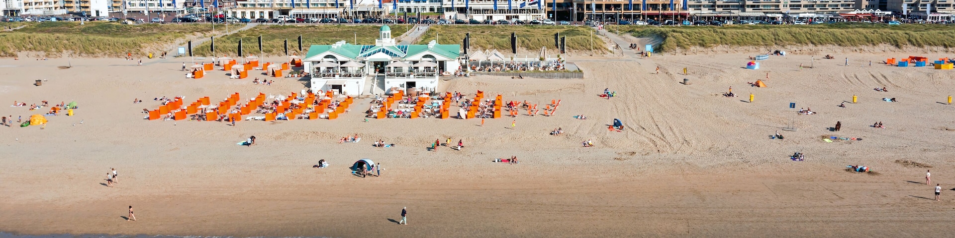 Uma praia com guarda-sóis laranja, uma torre de salva-vidas e edifícios ao fundo.