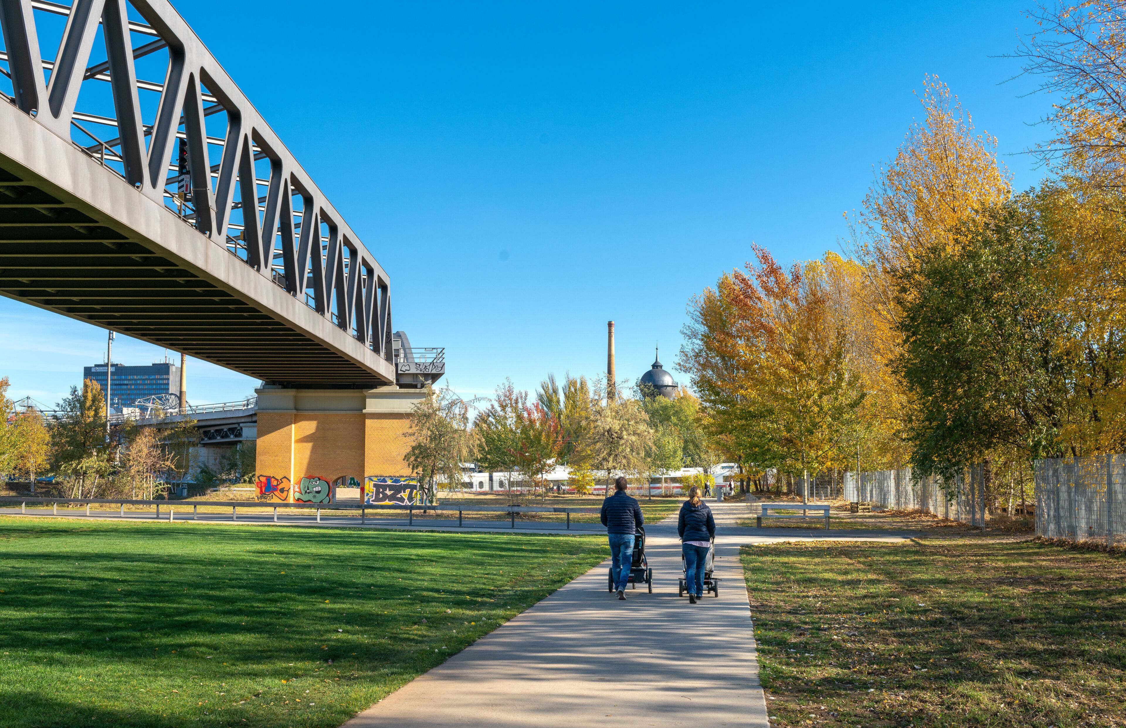 Um parque com uma trilha para pedestres, uma ponte, árvores de outono e um edifício com grafites.