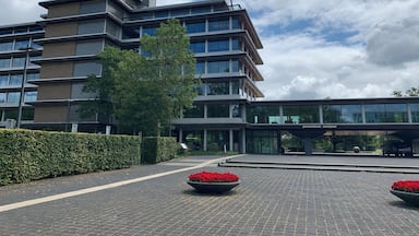 Um edifício moderno com relógio digital, uma árvore e vasos de flores vermelhas.