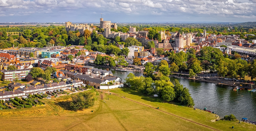 Uma cidade histórica com um castelo, rio e vegetação ao redor.