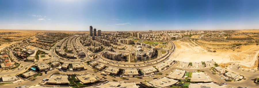 Paisagem urbana com uma rotatória central, áreas residenciais ao redor e paisagem desértica ao longe.