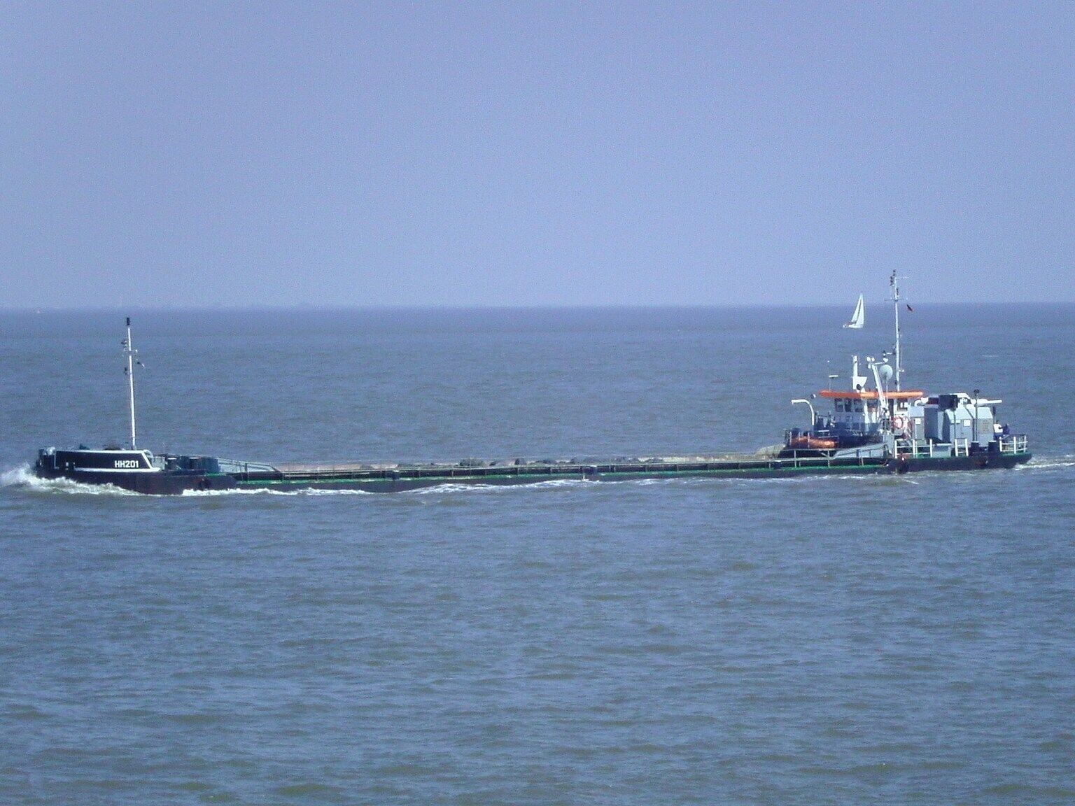 Um grande navio de carga com um rebocador menor ao seu lado, ambos navegando em um mar calmo.