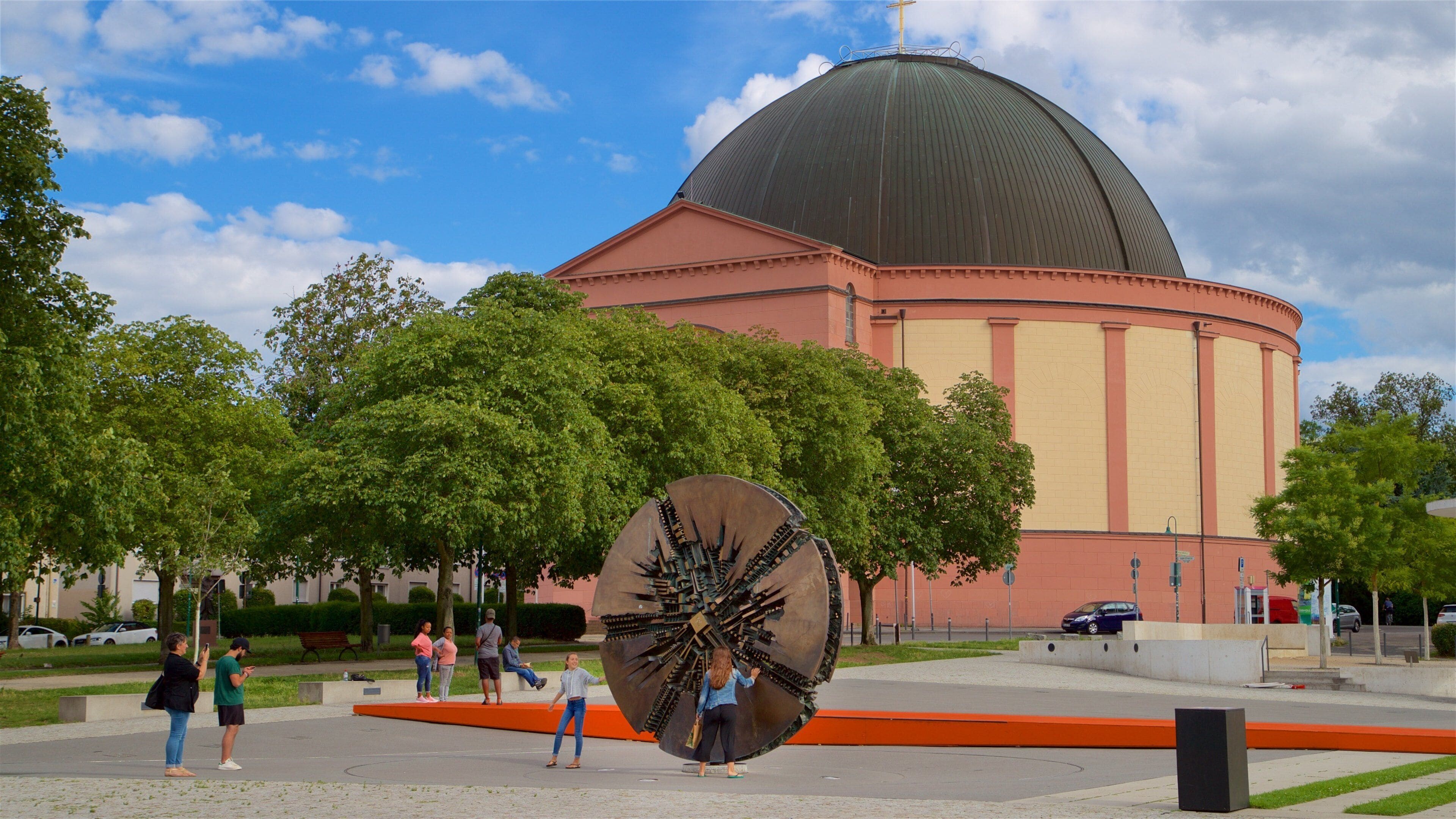 Uma grande escultura metálica em frente a uma igreja com cúpula.