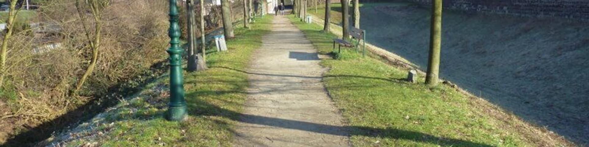 Um caminho pavimentado ao longo de um rio, ladeado por árvores e casas.