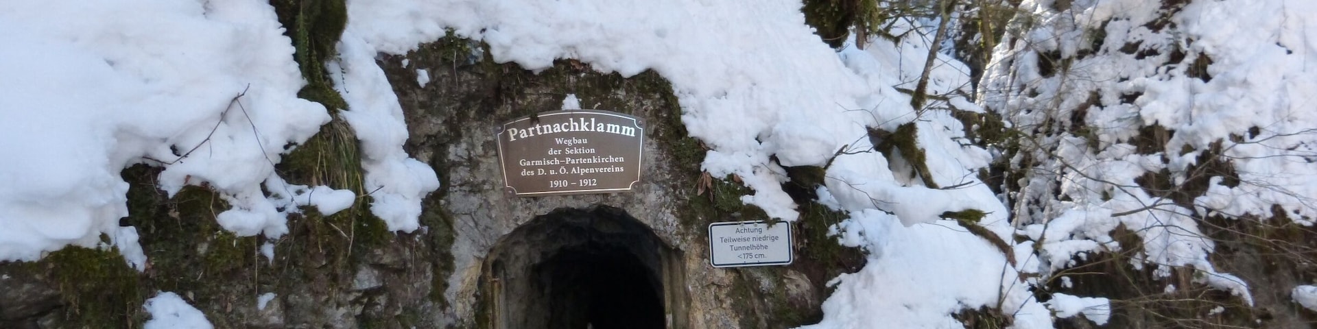 Entrada de um túnel coberto de neve, com uma placa que indica que foi construído entre 1910 e 1912.