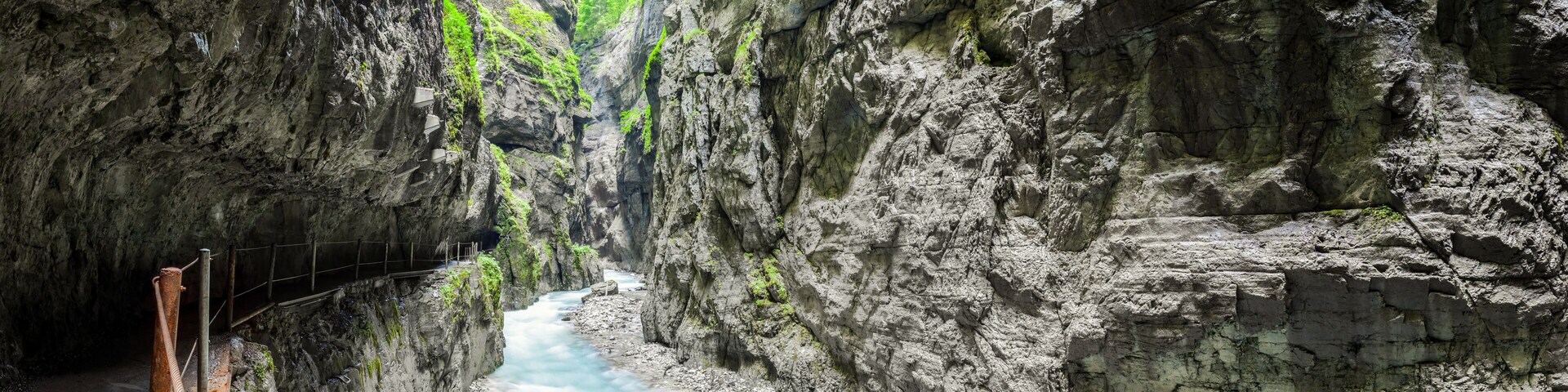 Um desfiladeiro estreito com um rio corrente, penhascos rochosos e uma passarela de madeira.