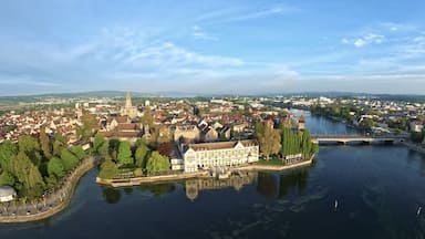 Uma cidade às margens de um rio, com uma torre de igreja imponente, um edifício que lembra um castelo e uma ponte.