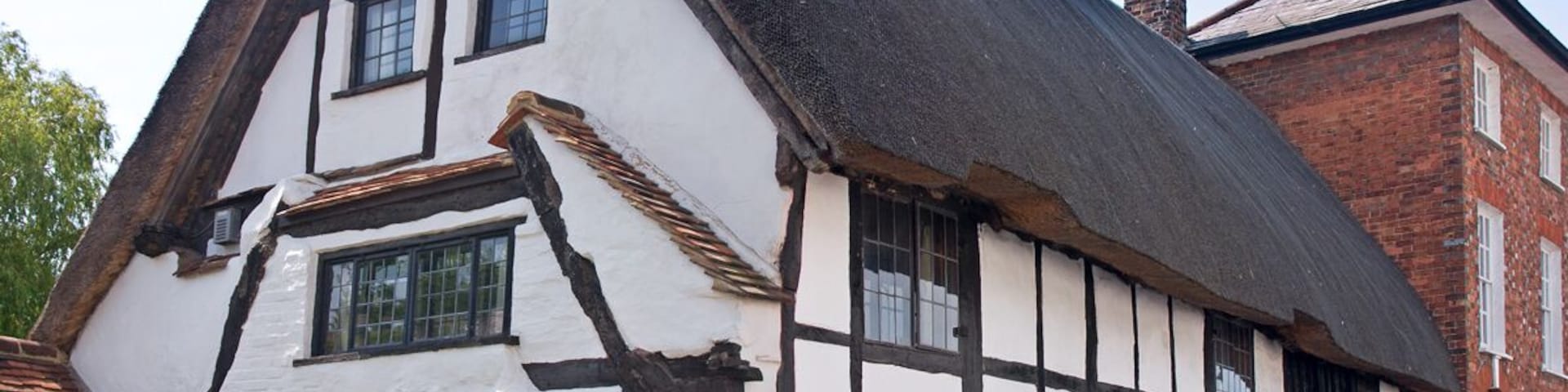 Uma casa tradicional de enxaimel com telhado de colmo íngreme e chaminé de tijolos.