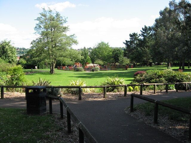 Um parque com um caminho pavimentado, bancos e um gramado bem cuidado.