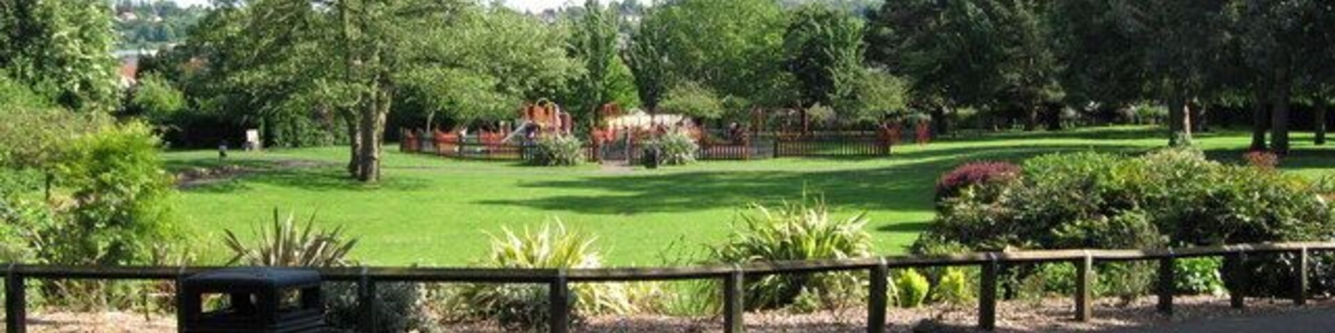 Um parque com um caminho pavimentado, bancos e um gramado bem cuidado.