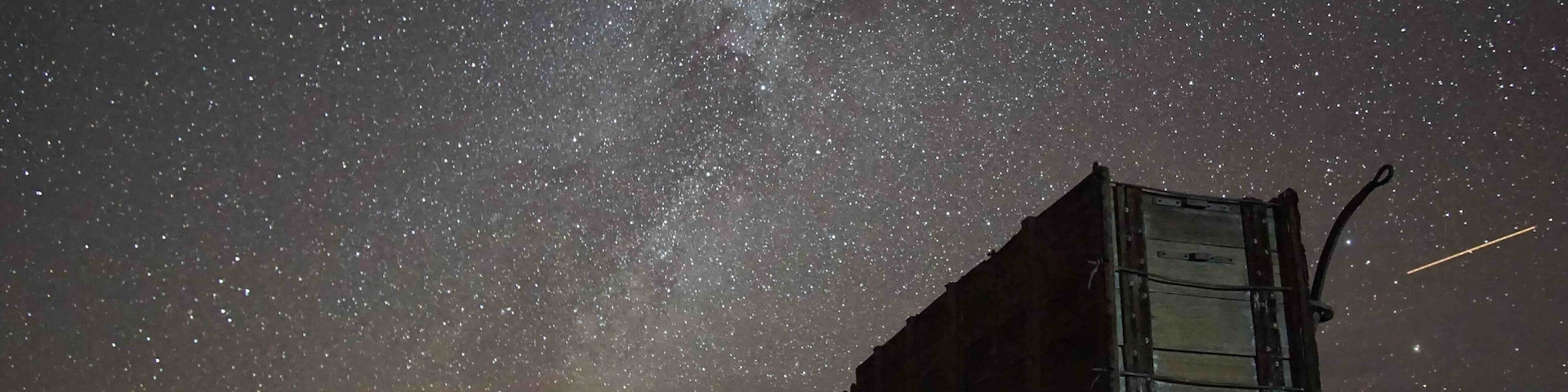 Céu estrelado à noite com uma caminhonete antiga estacionada em uma paisagem desértica.