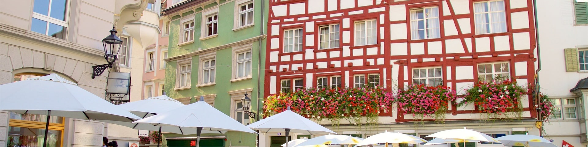 Rua europeia com edifícios coloridos em estilo enxaimel, cafés ao ar livre e pessoas jantando.