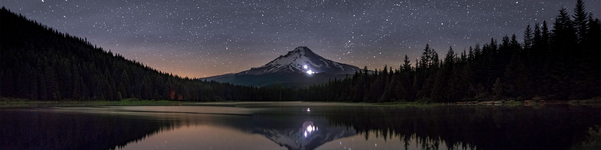 Um céu estrelado sobre um lago calmo, com uma montanha ao fundo.