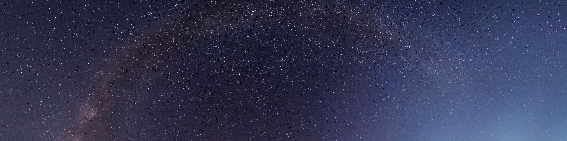 Céu noturno estrelado com a Via Láctea visível e uma lua crescente.