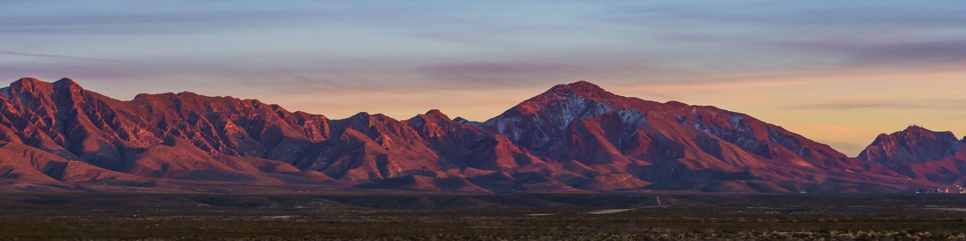 Paisagem desértica com montanhas de rocha avermelhada e vegetação escassa.