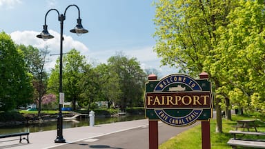 Placa de boas-vindas para Fairport na Trilha do Canal Erie, com um banco e um poste de luz por perto.
