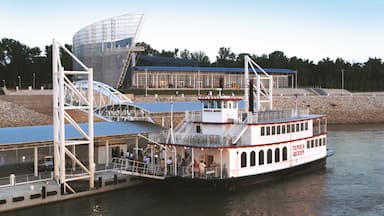 Um barco de recreio chamado "Tunica Queen" atracado em um cais com uma ponte de vidro e uma área coberta.