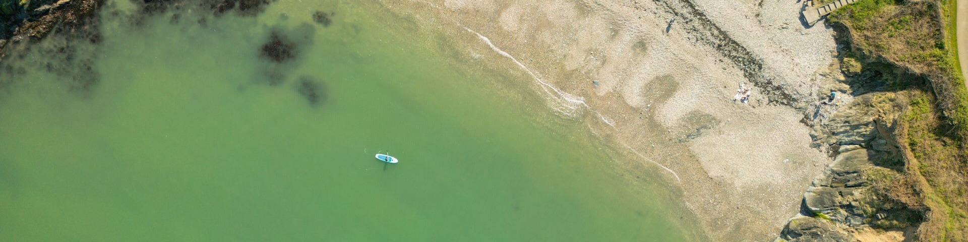 Vista aérea de uma área costeira com uma grande lagoa verde, falésias rochosas e um pequeno barco na água.
