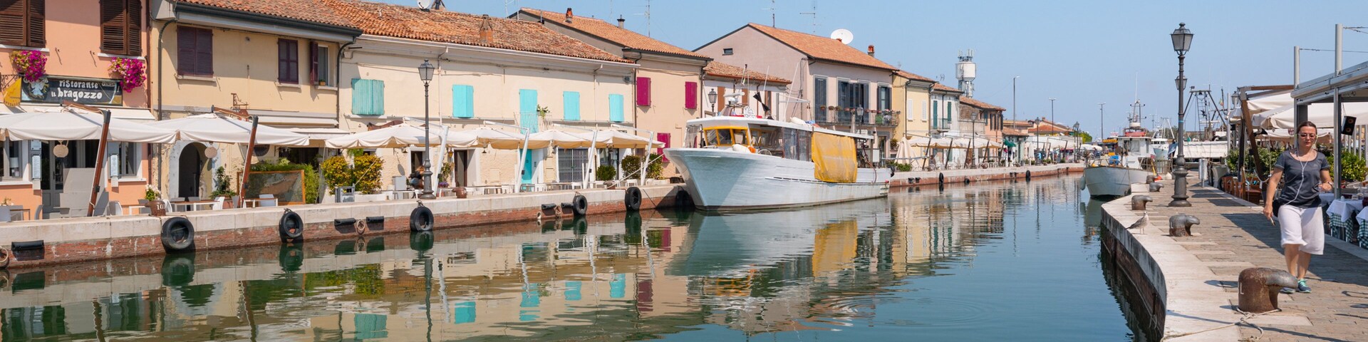Um canal com barcos, edifícios à beira-mar e uma passarela para pedestres.