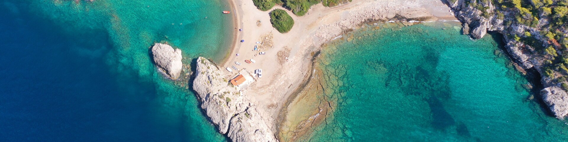 Vista aérea de uma área costeira com águas turquesa cristalinas, costas rochosas e um pequeno edifício perto da orla.