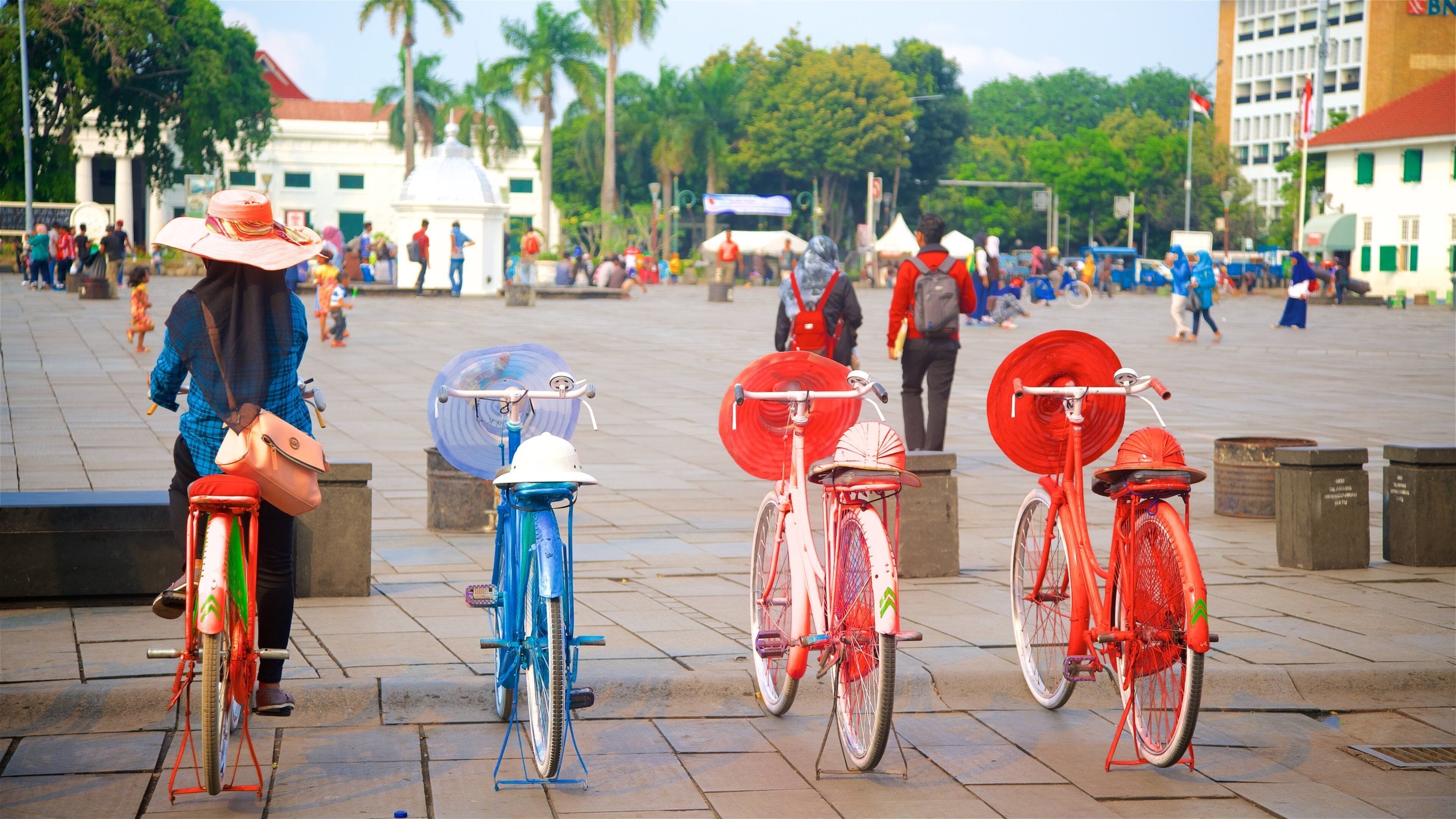 Uma praça pública com bicicletas, palmeiras e edifícios ao fundo.