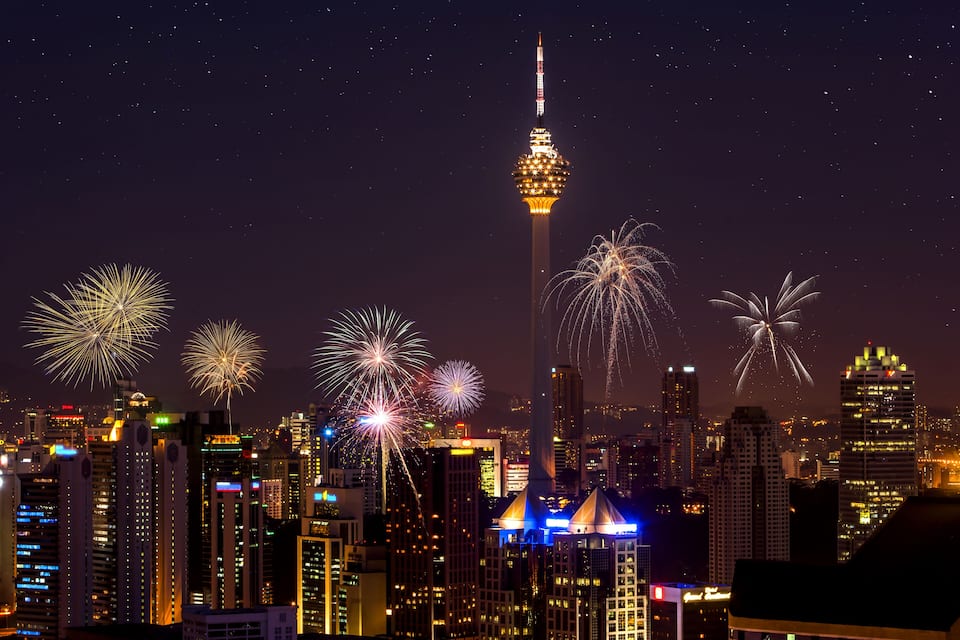 Silhueta urbana noturna com fogos de artifício e uma torre imponente.