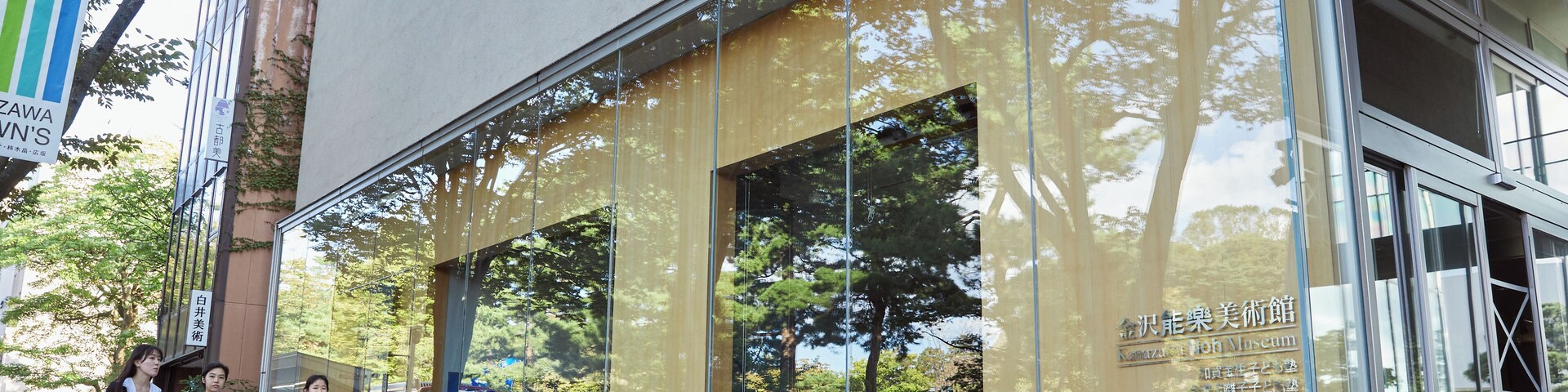Um edifício moderno com grandes janelas de vidro refletindo árvores e o céu.