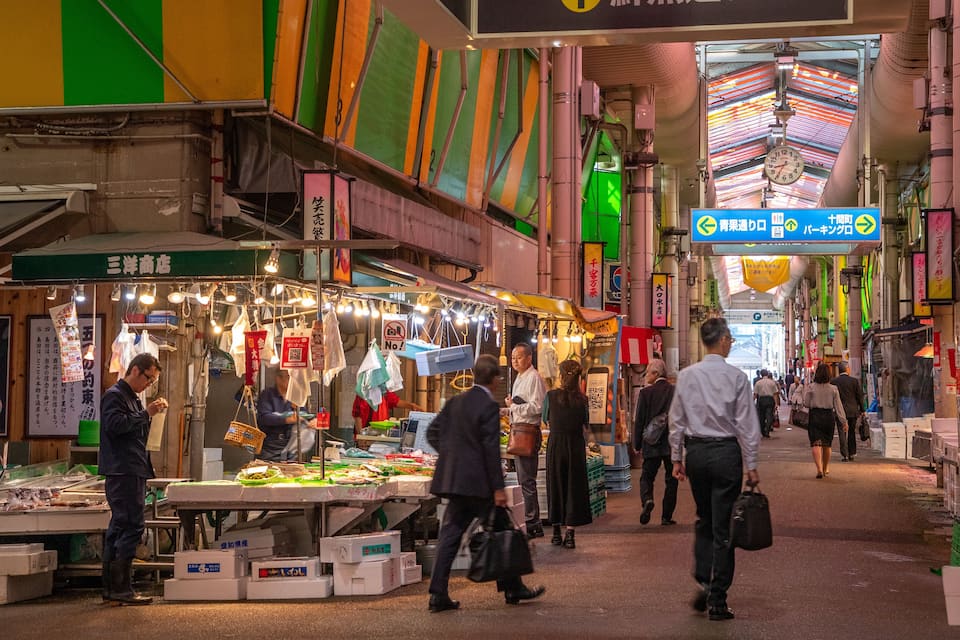 Um mercado interno movimentado com vários quiosques vendendo produtos, iluminado por luzes penduradas.