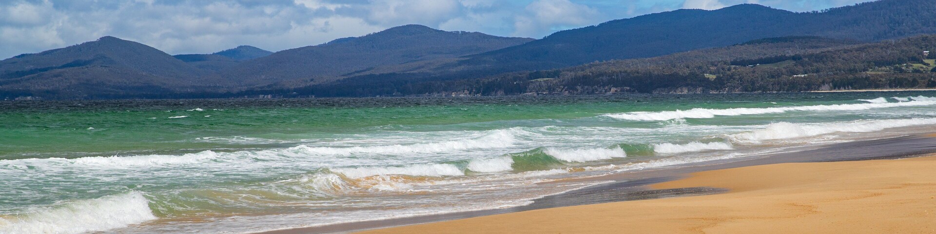 Uma praia com ondas, montanhas e céu parcialmente nublado.