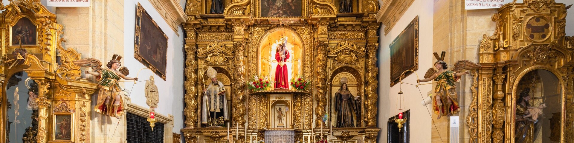 Interior de igreja ornamentado, com detalhes dourados, um altar central e estátuas religiosas.