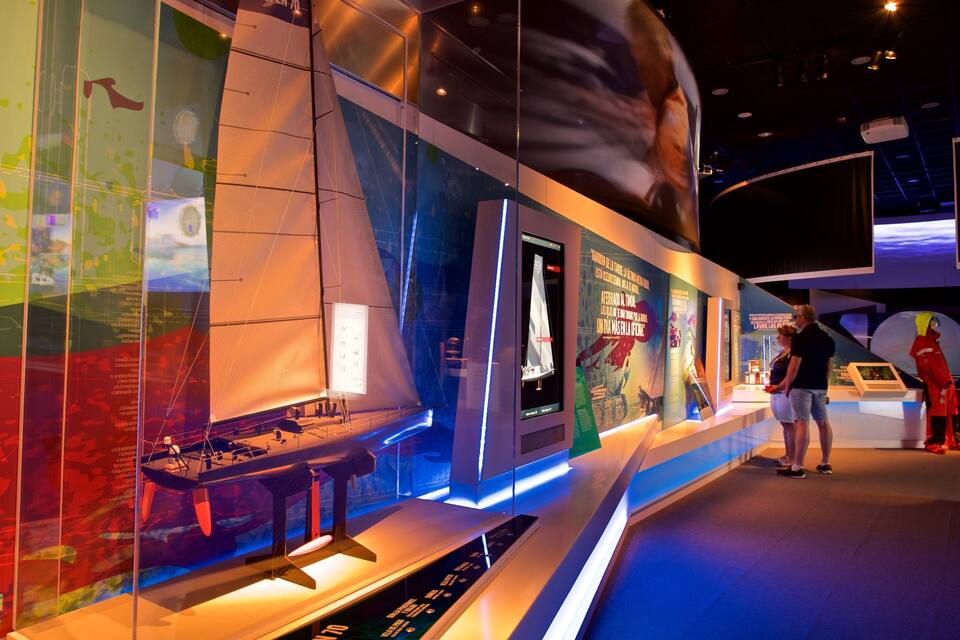 Uma exposição de museu com uma maquete de veleiro, painéis informativos e um cartaz grande.