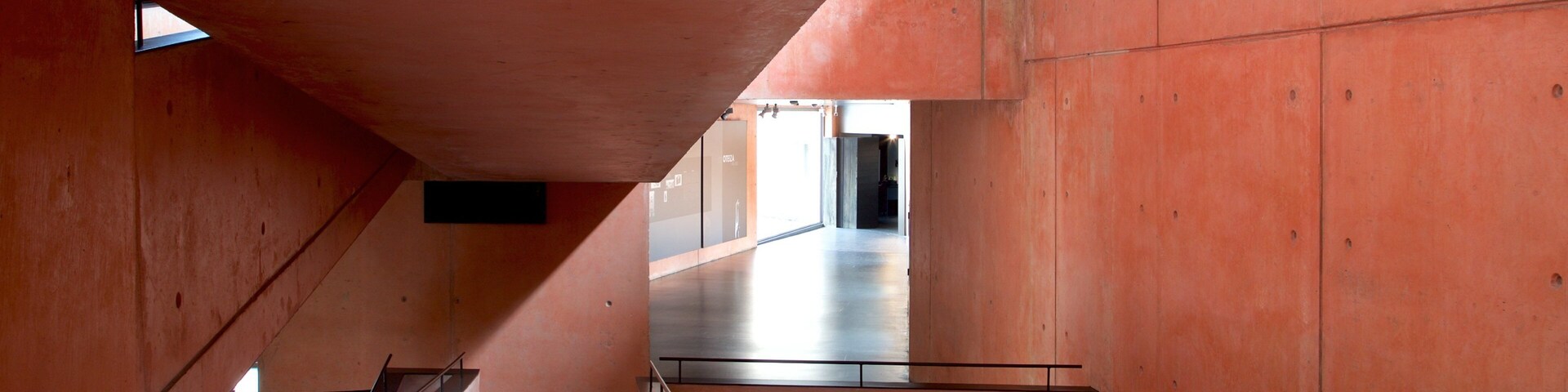 Um interior arquitetônico moderno com teto inclinado, guarda-corpos de metal e piso refletivo.