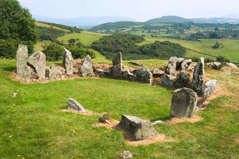 Um círculo de pedras em um campo gramado, com colinas ondulantes ao fundo.