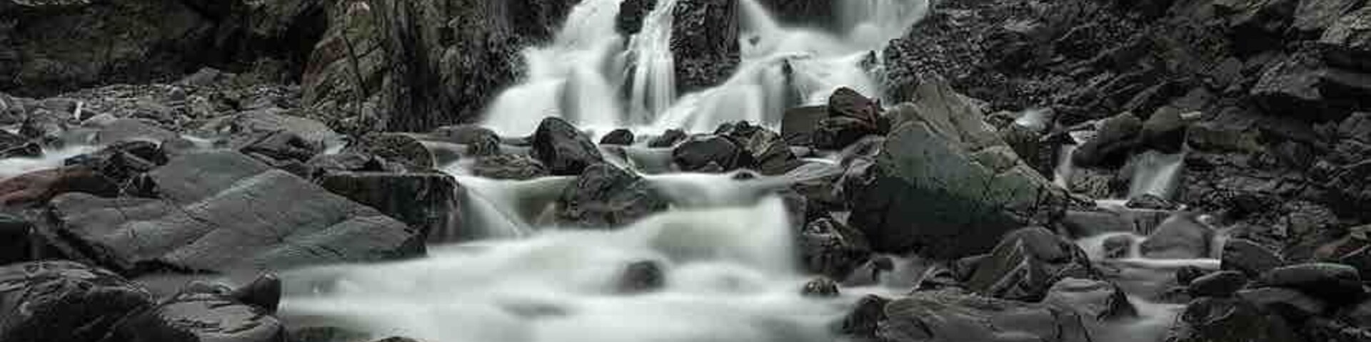 Uma cascata desce sobre rochas em um desfiladeiro rochoso.