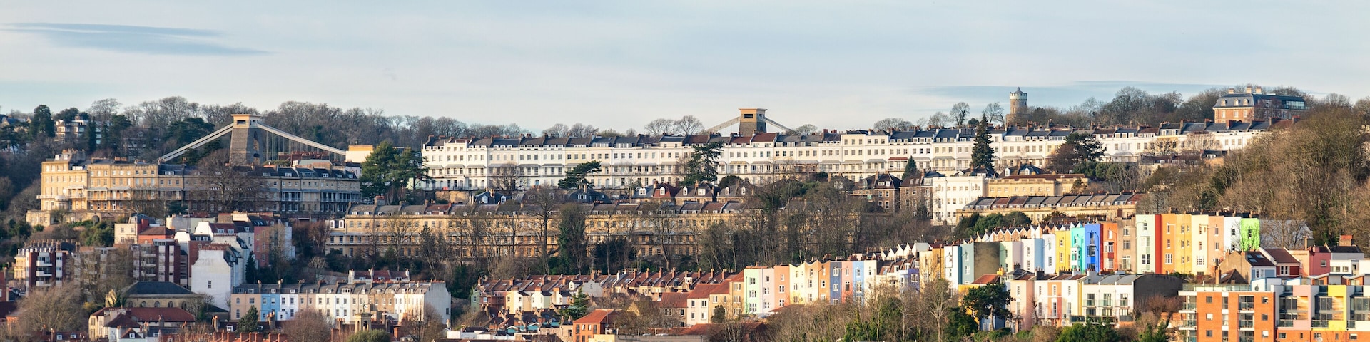 Paisagem urbana com uma ponte imponente, edifícios históricos e uma colina com uma torre.