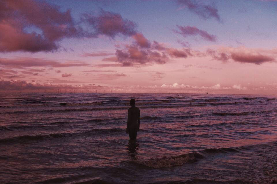 Uma pessoa em pé no oceano durante o pôr do sol.