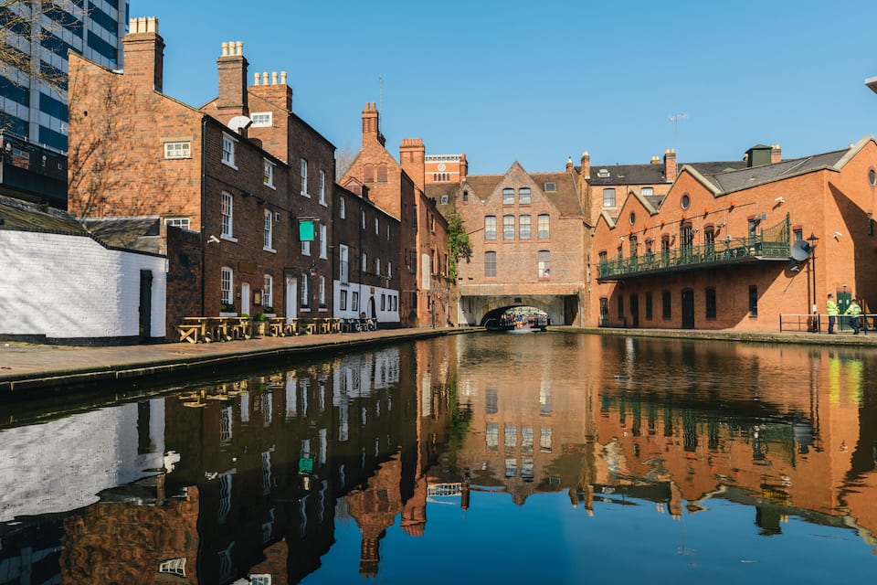 Um canal com edifícios refletidos na água, uma ponte e um céu azul límpido.