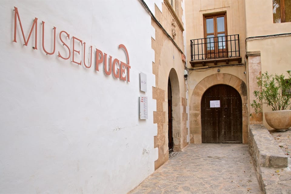 A narrow cobblestone street with a white building labeled "MUSEU PUGET" and a wooden door.