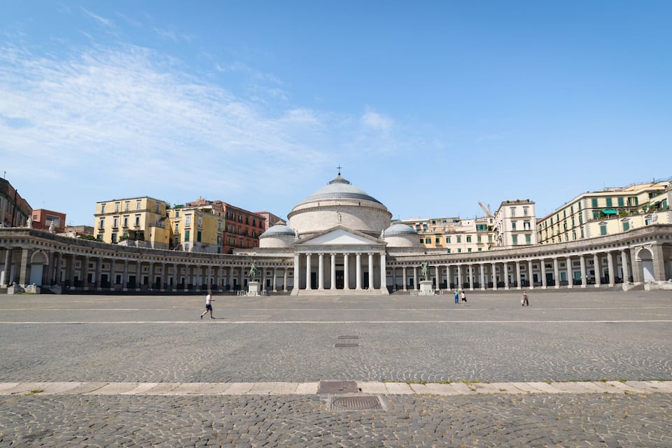 Uma grande praça aberta com um edifício histórico, com cúpula e colunas.