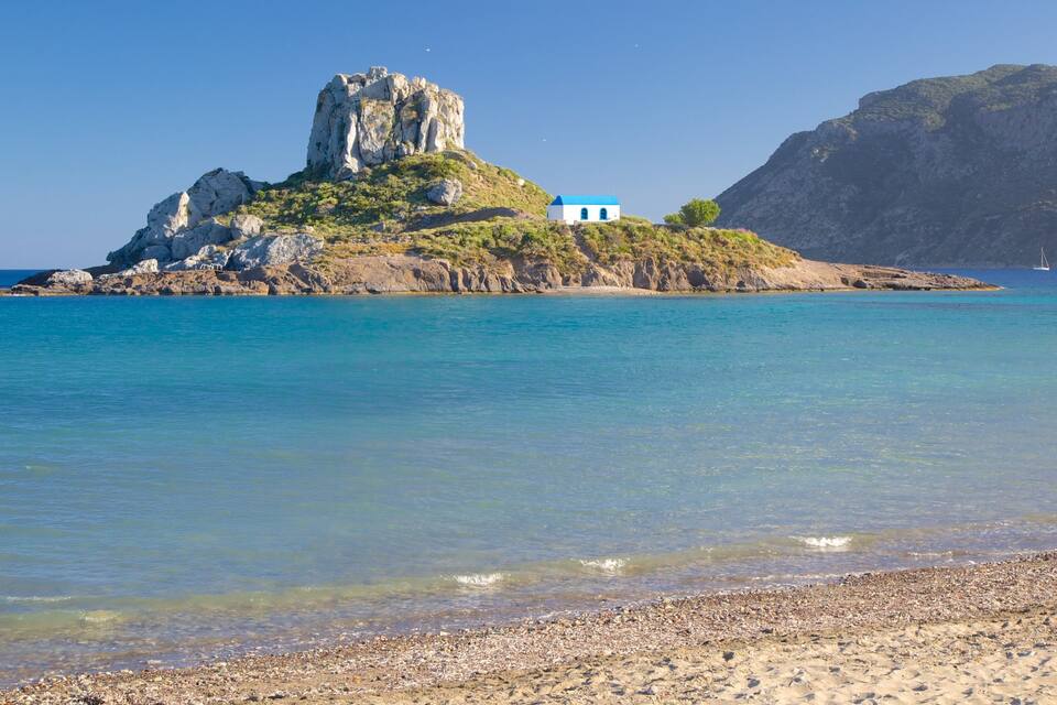 Ilha rochosa com um edifício branco e uma grande formação rochosa.