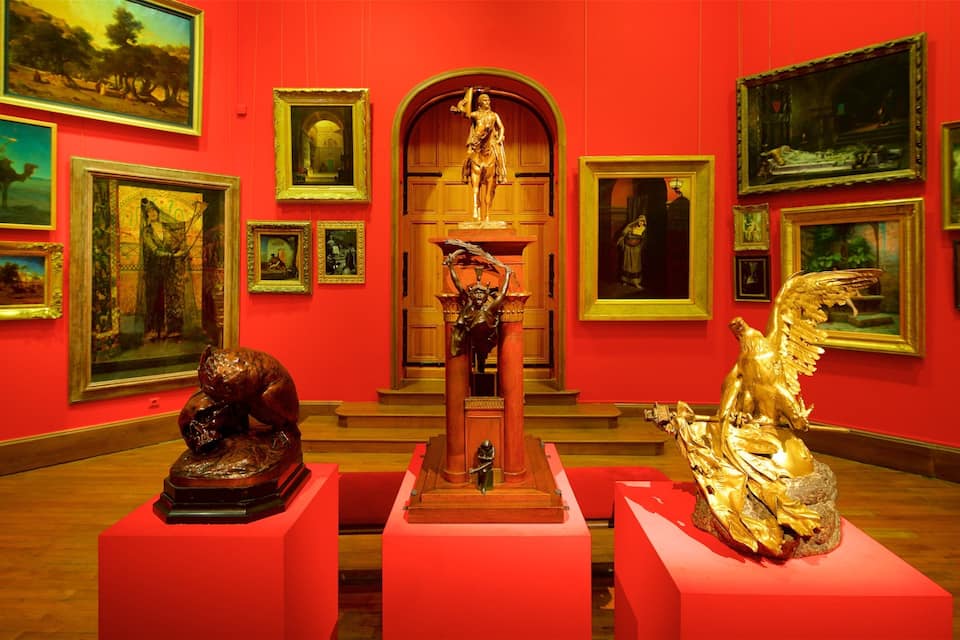 Um museu com paredes vermelhas e diversas pinturas e esculturas expostas.